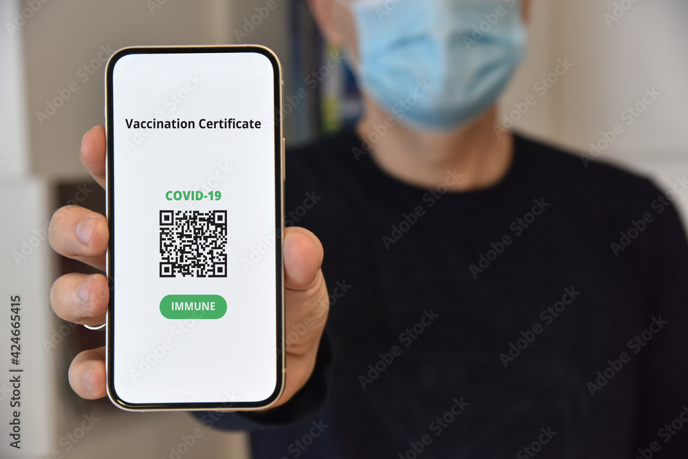 Man with face mask holding mobile phone with digital green certificate ...