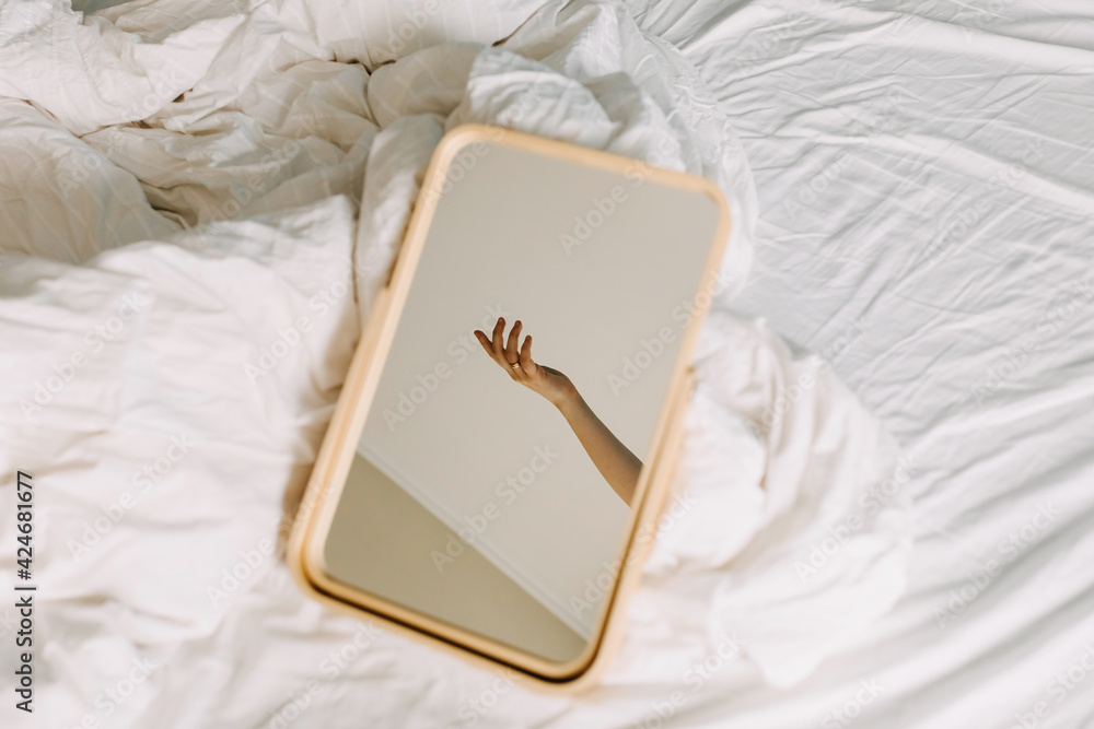 Female hand reflected in a mirror on white bed sheet background. Stock ...