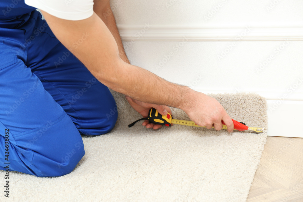 Worker with cutter knife and measuring tape installing new carpet ...