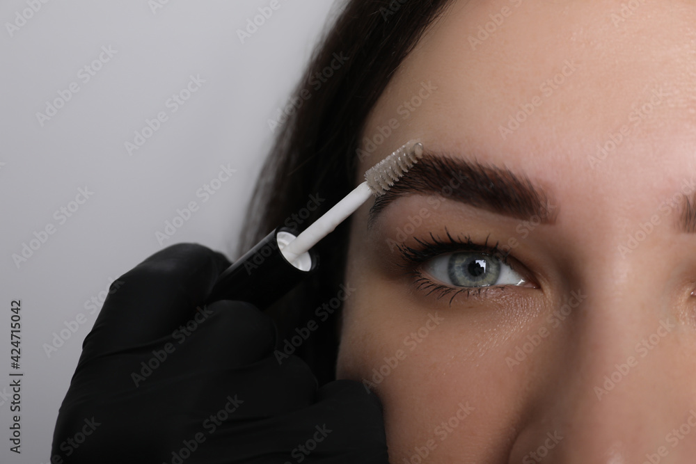 Beautician fixing woman's eyebrows with gel after tinting on light grey ...