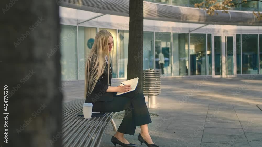 Successful young woman taking notes outdoors. Side view of elegant ...