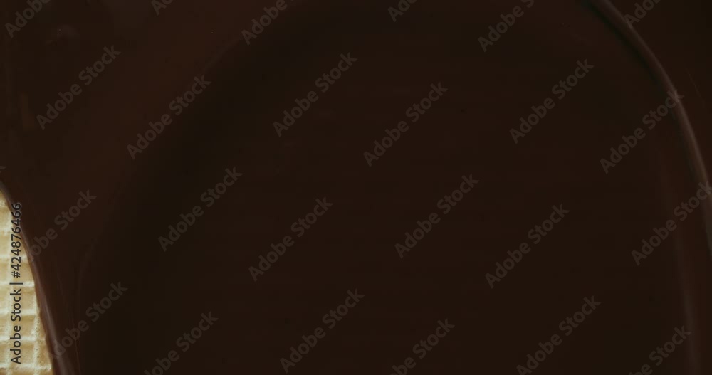 Close-up macro shot hot melted liquid chocolate flows over wafer ...