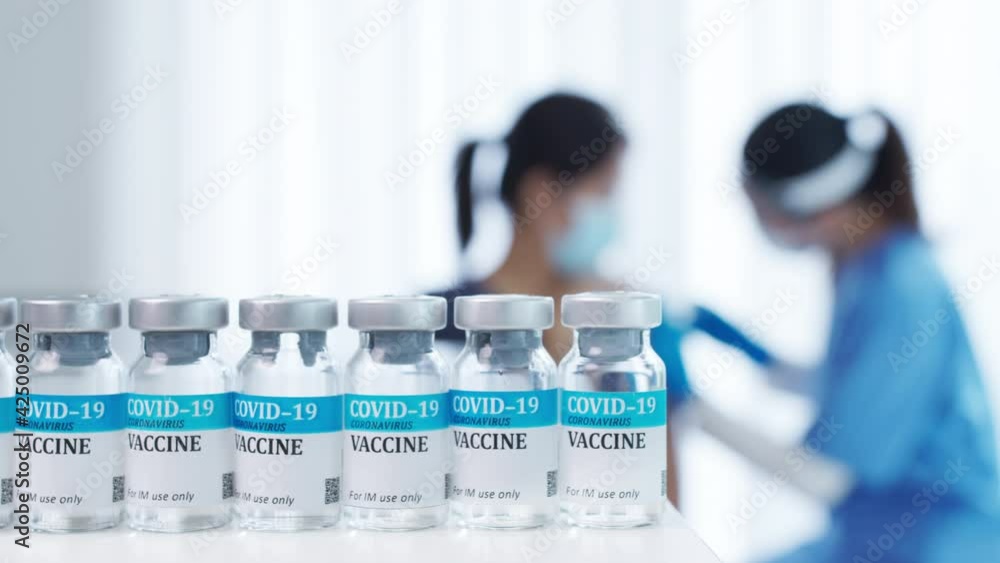 Many vaccine vial bottle in background of young female asian doctor, scrub nurse hold syringe ...