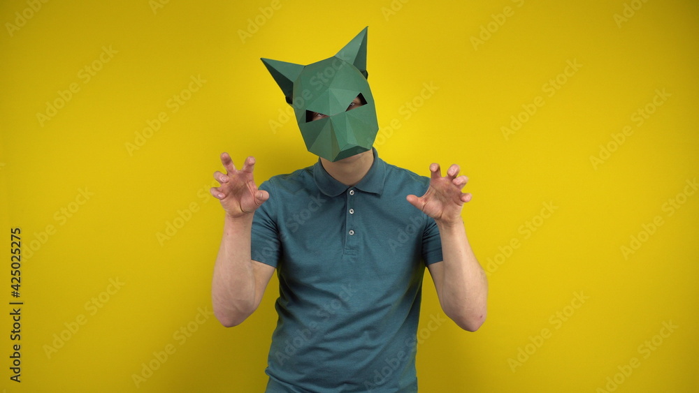 A young man in a cardboard jackal mask depicts an animal and looks at ...