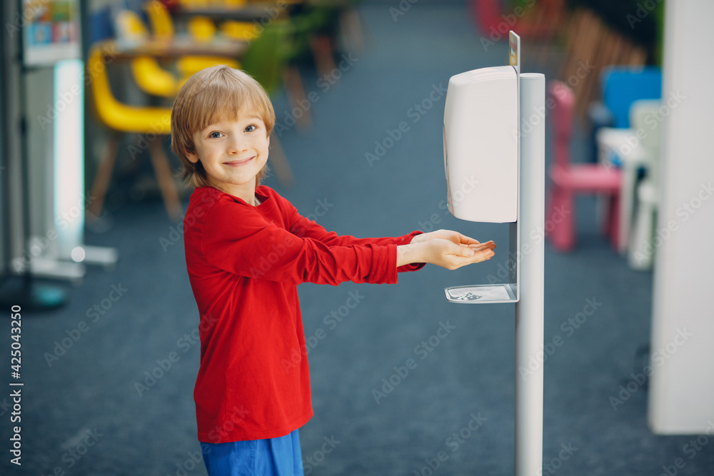 Child smiling boy kid using automatic alcohol gel dispenser spraying on ...