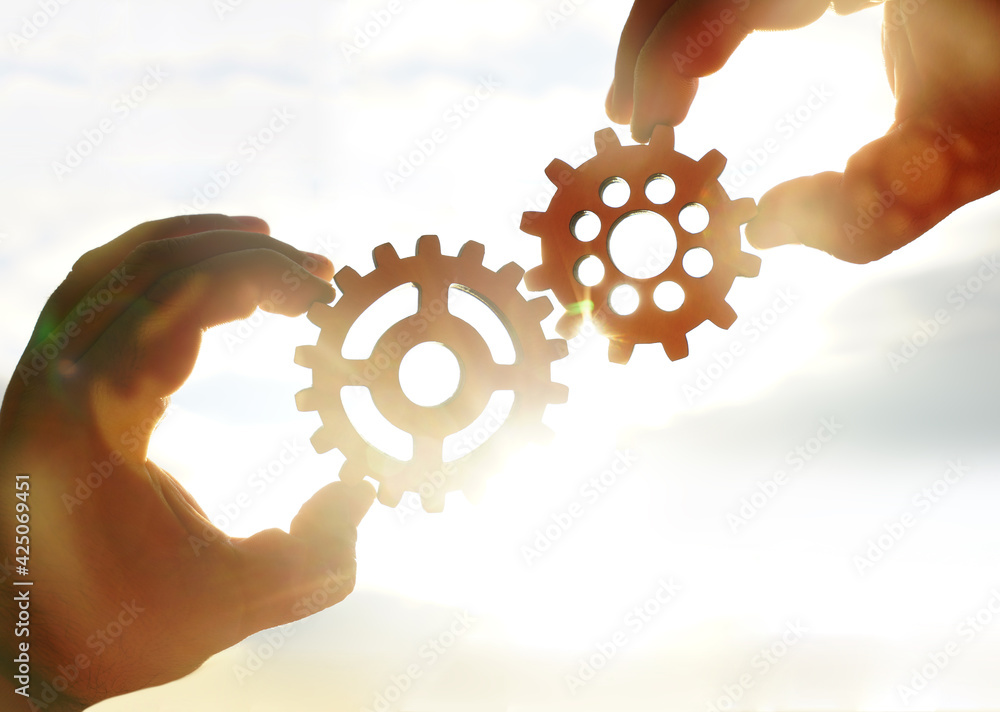 Male hand holding two wooden cog gear wheel on sunny sky background ...