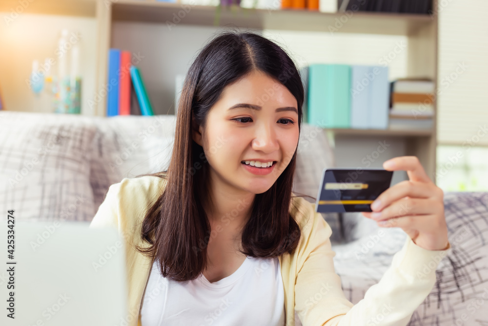 Young asian woman using plastic credit card and satisfied to credit card, sitting at living room ...