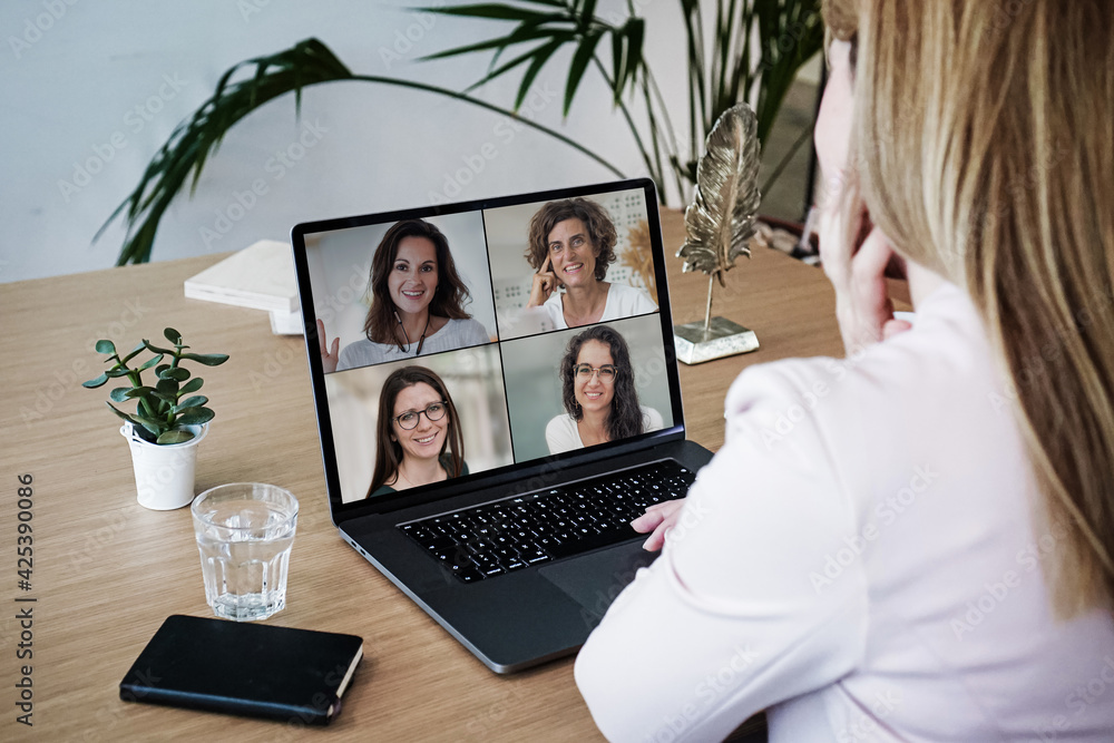 back of a remote online coaching woman sitting on her work desk infront ...