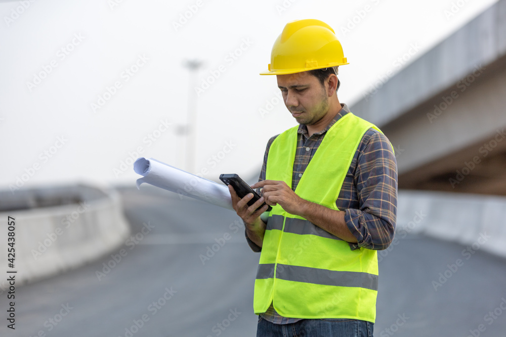 construction worker holds blueprint and typing a message on smart phone ...
