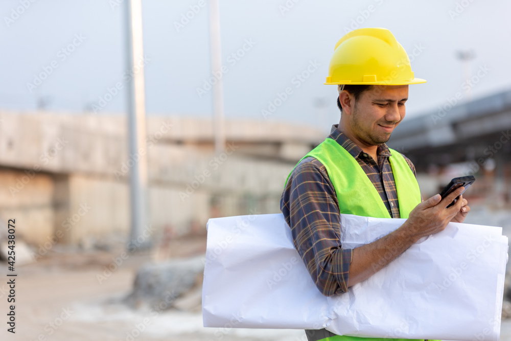 construction worker holds blueprint and typing a message on smart phone ...