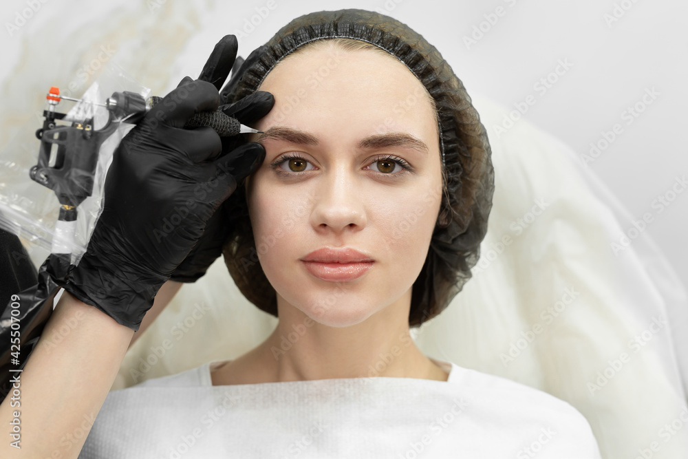 Concept of microblading eyebrows. The cosmetologist performs the procedure of permanent makeup ...