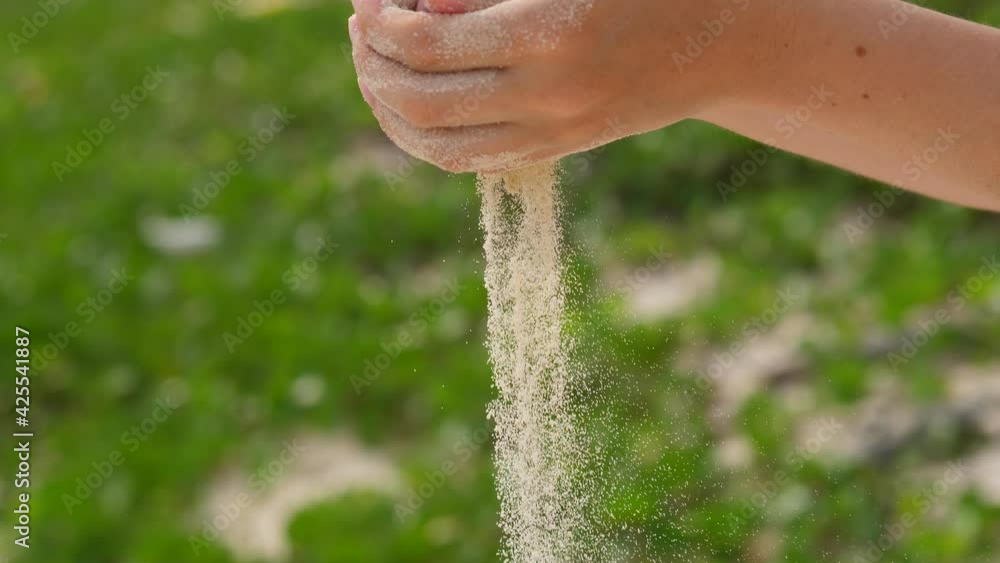 Stream of sand grains pour down from cupped hands of woman, green ...