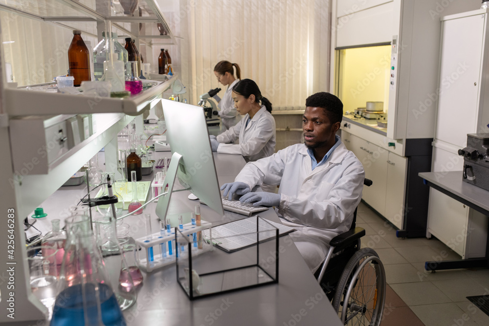 African disabled scientist sitting in wheelchair at the table and ...