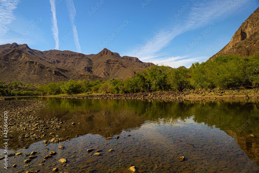 Reflection of a hill and bushes in the water of the Yaqui River as it ...
