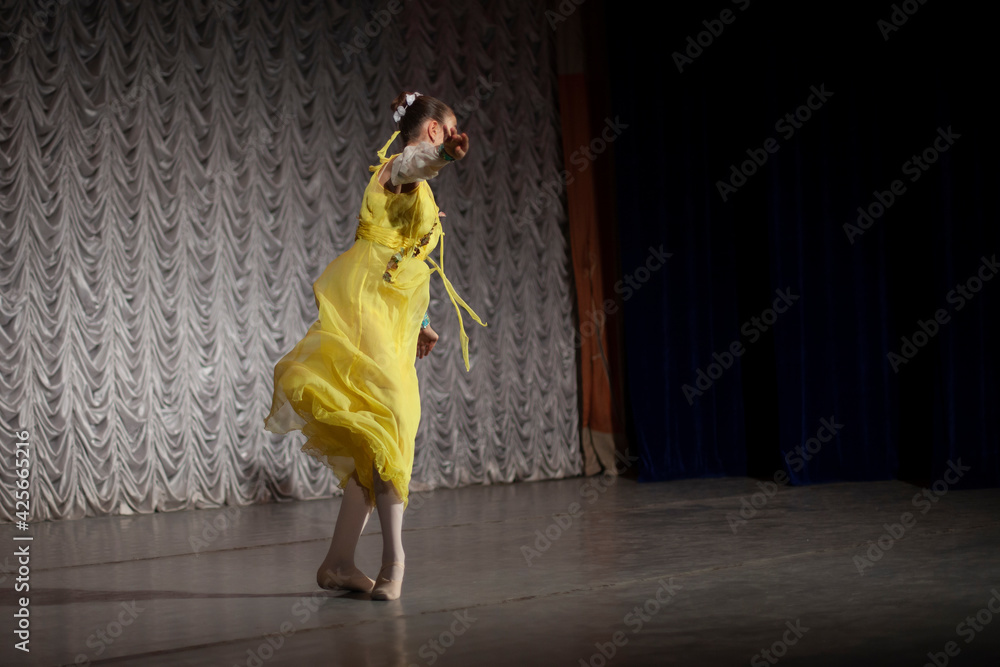 Girl in a yellow dress.The girl is dancing on stage. Dancer's movements ...