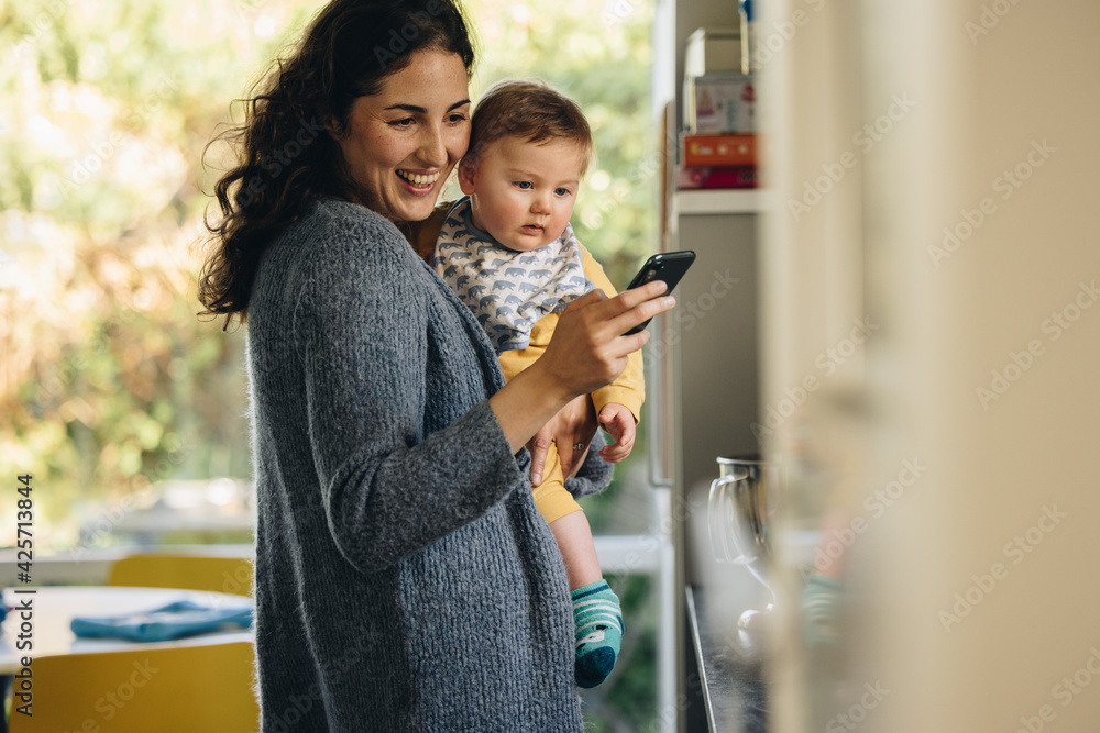 Mother carrying baby texting on her cell phone Stock Photo | Adobe Stock