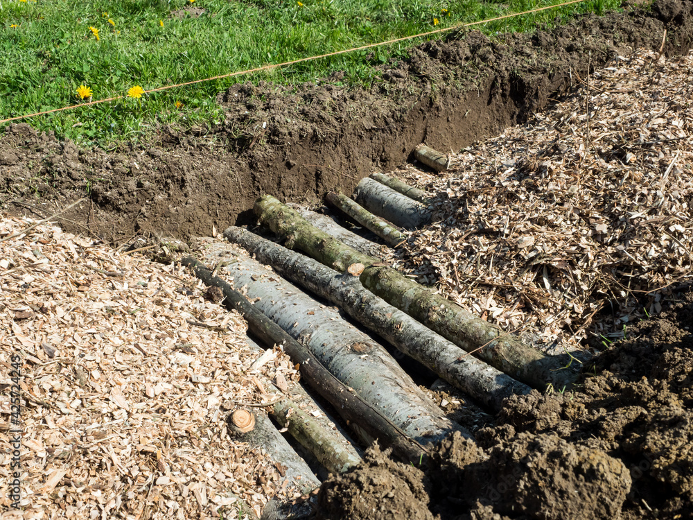 Permaculture trench with wood logs and shredded wood and grass in ...