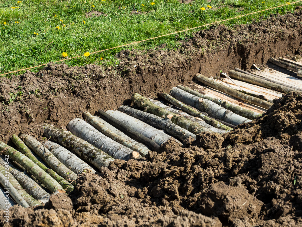 Permaculture trench construction with half long logs of wood with grass ...