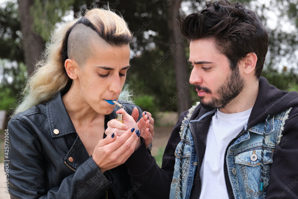 Young punk couple lighting up a cigarette in a park. Rock and roll ...