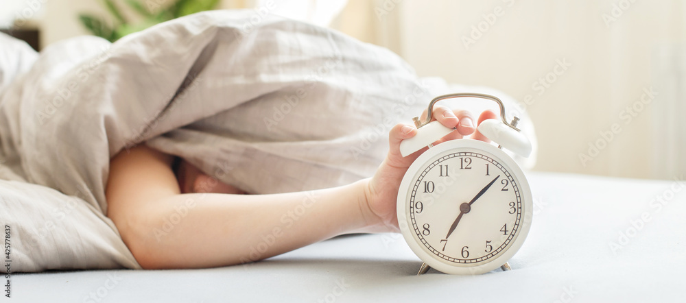 boy lying on the bed and stopping alarm clock in morning. childs hand ...