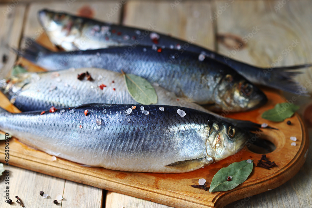 Salted herring of spicy salting. Spices and salt. Herrings with head and tail on a wooden board ...