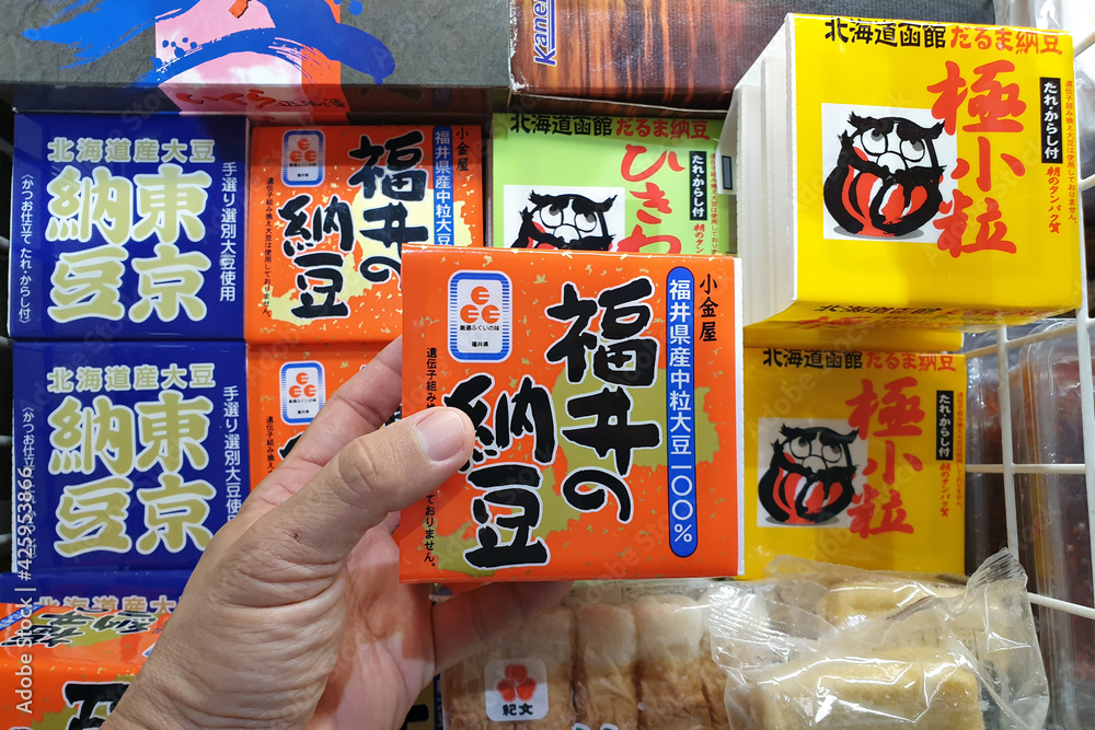 Foto de Close up hand holding a pack of Natto in a grocery store ...
