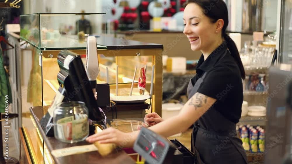 a girl cashier in an apron counts money from the cash register, partly ...