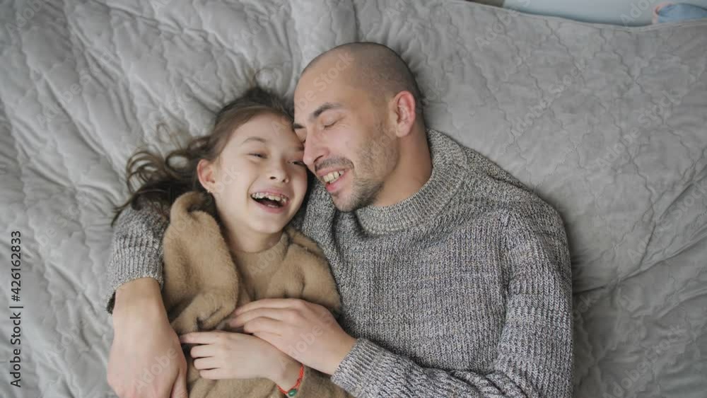 Father and daughter laughing and bonding in bed. Daddy and his little girl spending bed time at ...