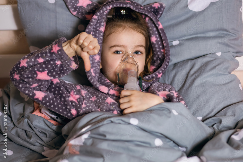 A little girl in a hooded robe is ill and is lying on the bed with an ...