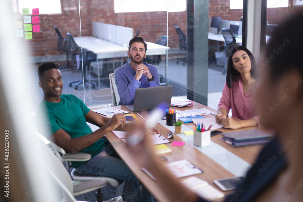 Diverse group of creative colleagues in meeting room listening ...
