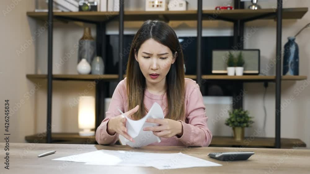 Slow motion frustrated Asian woman looking at the paper bills upset throwing crumpled paper away ...