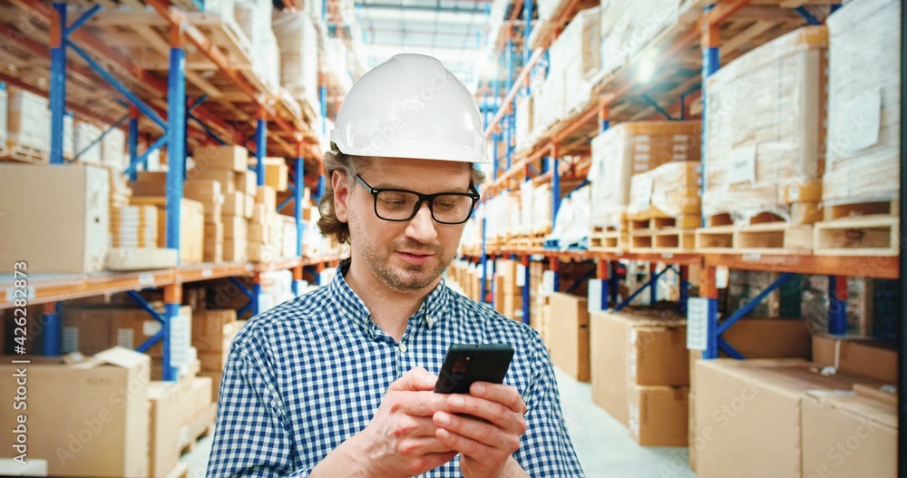 Warehouse manager in glasses and white helmet standing on background of ...