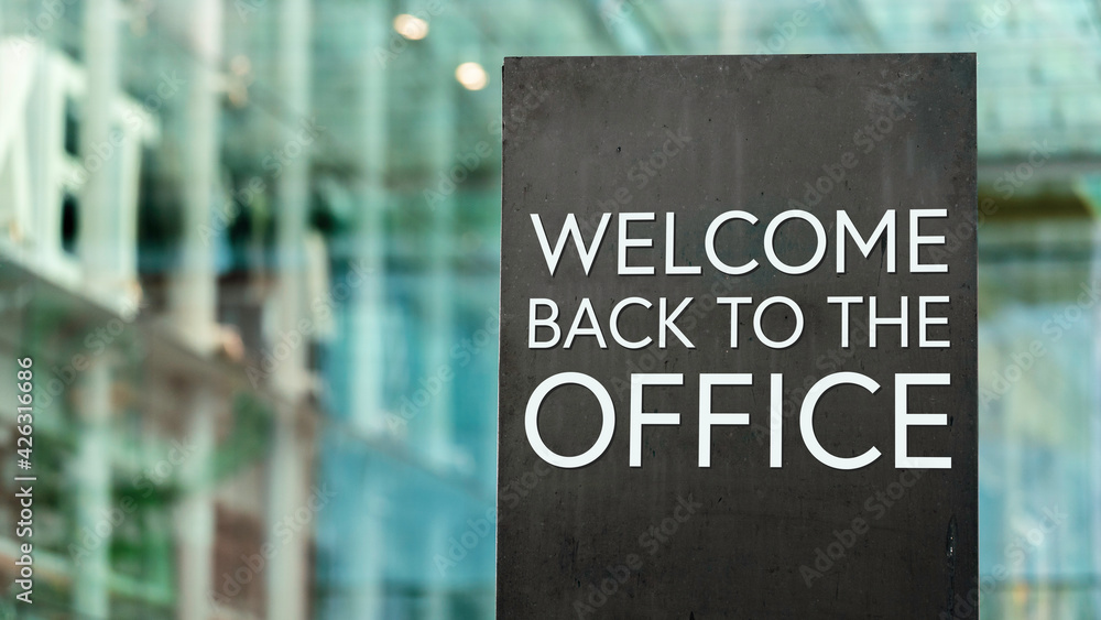 Welcome back to the office on a city-center sign in front of a modern ...
