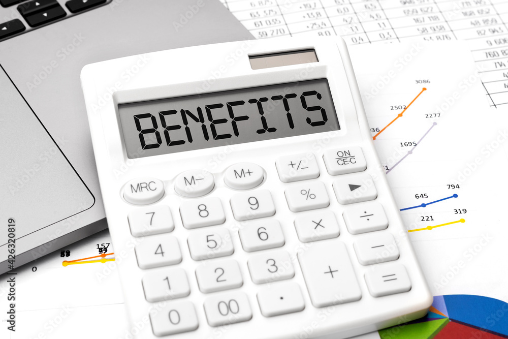 Word BENEFITS on calculator on laptop with paper with charts. Top view ...
