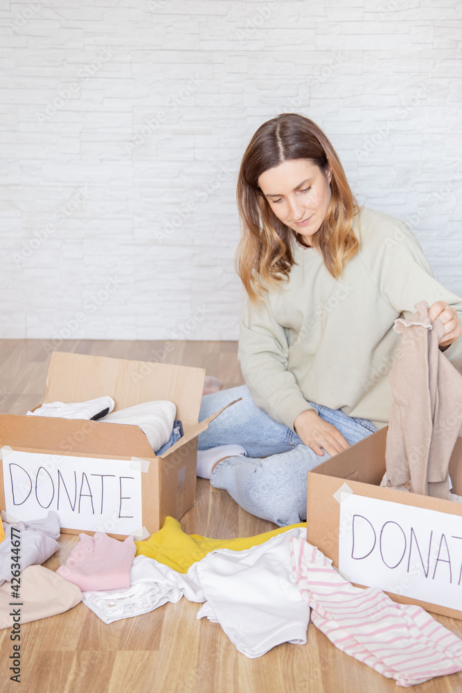 Young woman sitting on floor and packing clothes in cartoon box for ...