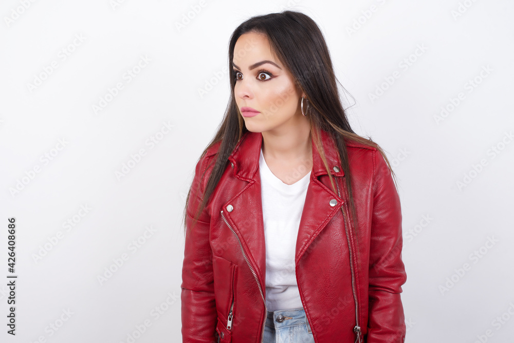 young beautiful brunette woman wearing red biker jacket over white wall ...
