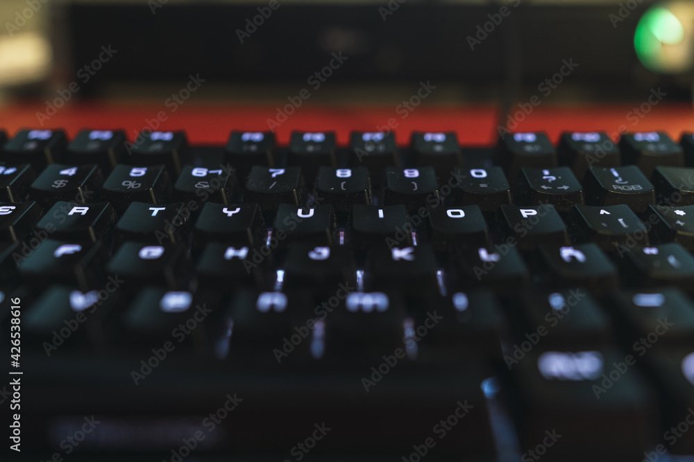 Closeup of the middle part of a black keyboard with white rgb lights on ...