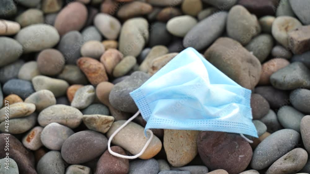 Close-up used Face mask on pebble beach, have started polluting water ...