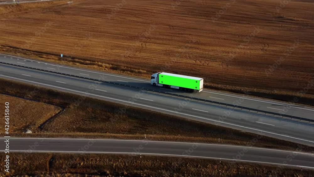 Truck with green screen on trailer drives along the highway in the rays ...