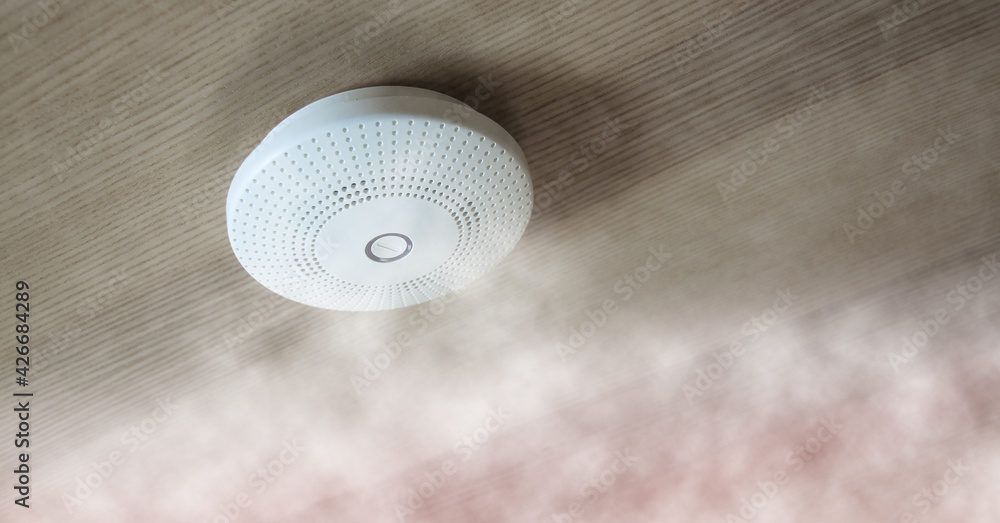 modern smoke detector on wooden ceiling with white smoke and fog ...