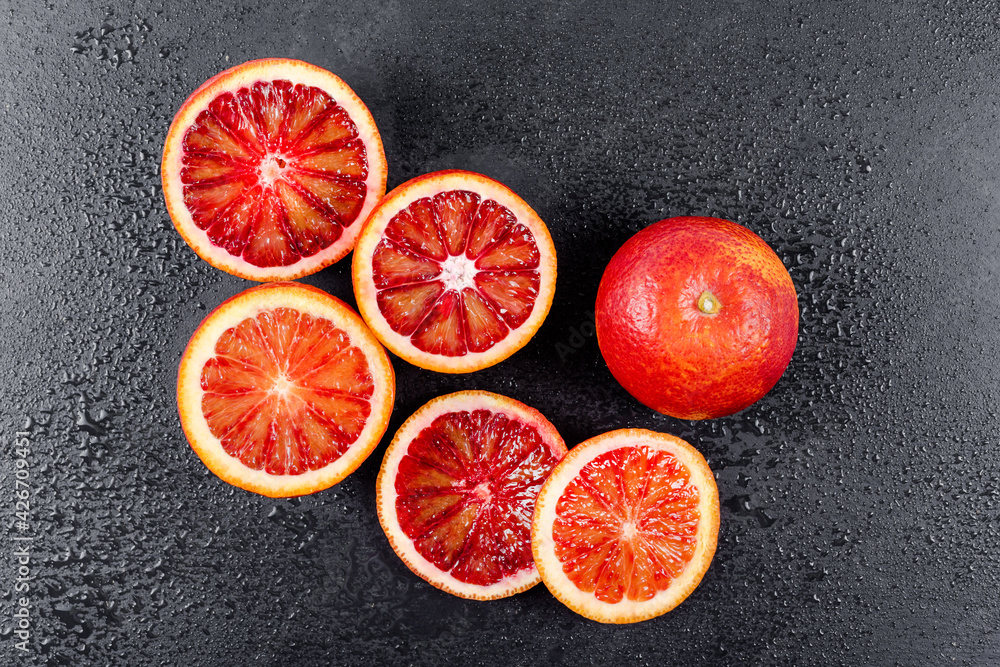 Bloody oranges whole, cut in half and sliced on black slate board with ...