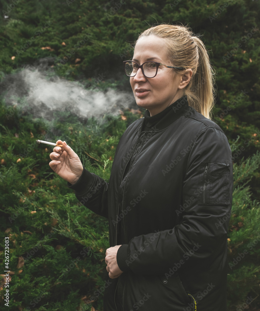Blonde polish woman in her 40s smoking cigarette outside in the forest ...