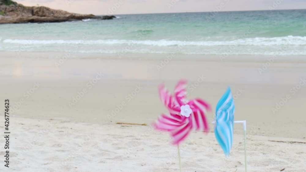 Pink and blue pinwheels toy spinning on white sand beach, two colorful ...