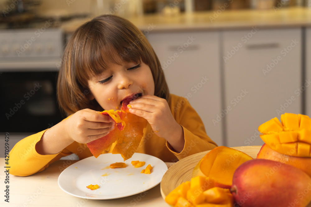 Cute child girl is happy to eat mangoes. Schoolgirl joy tasty eating ...