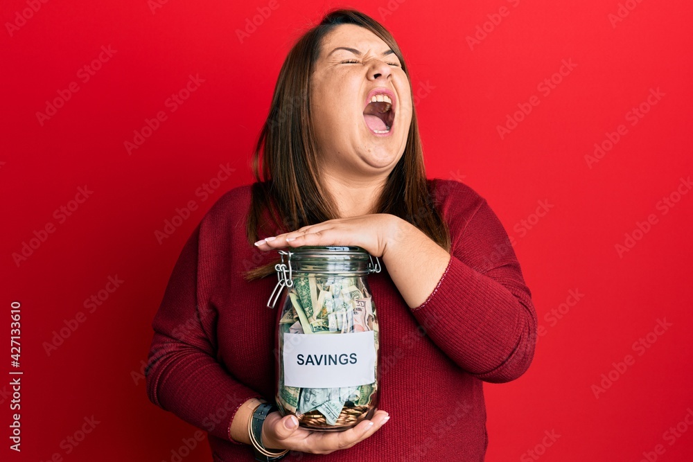 Beautiful brunette plus size woman holding jar with savings angry and ...
