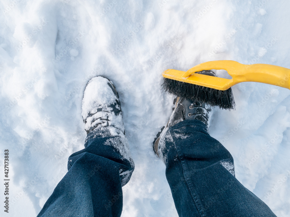 A man in jeans stands in the snow and sweeps off snow from his legs and ...