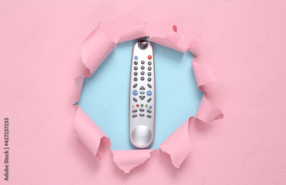 Tv remote through a torn hole on a blue-pink pastel background. Concept ...