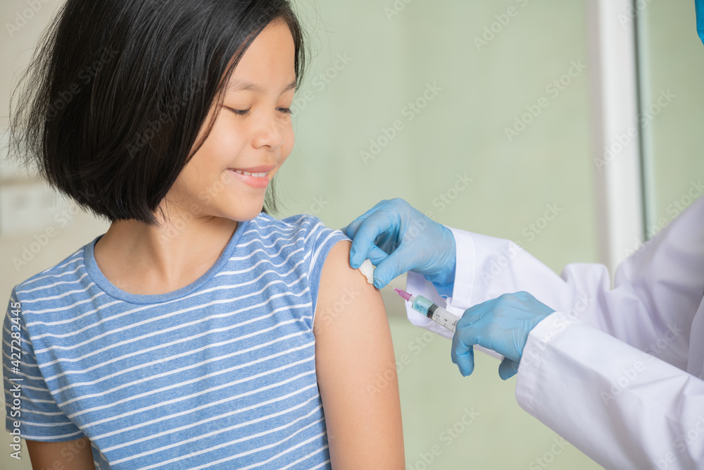 Asian little girl in doctor's office is vaccinated. Syringe with ...