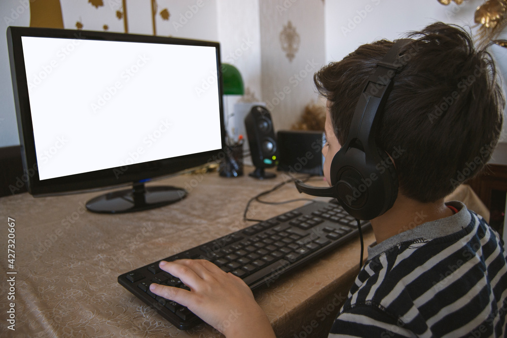 boy playing computer games at a desk at home and wearing headphones ...