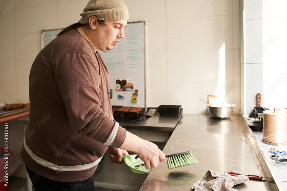 Male baker cleaning with brush table of the flour while tidy his ...